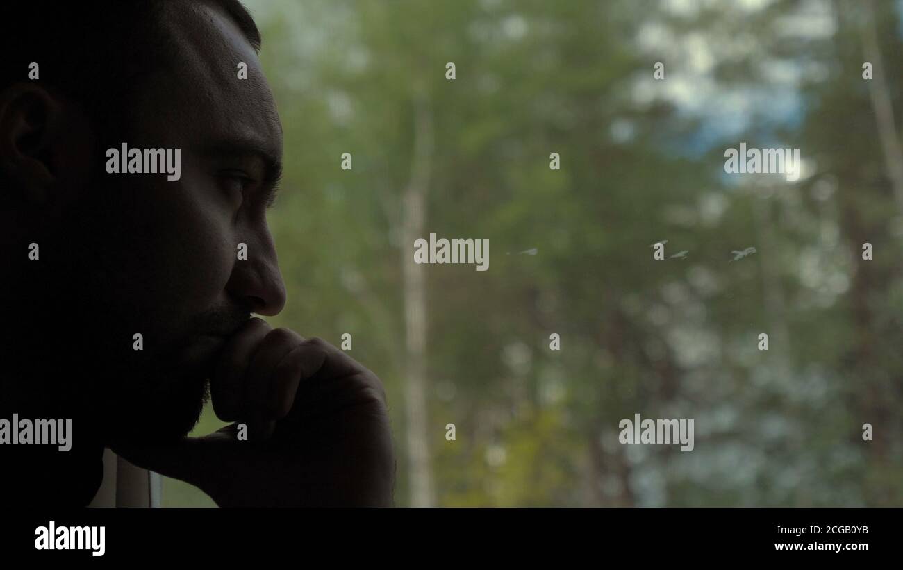 Man looking out window with chin on hand in a train, serious expression ...