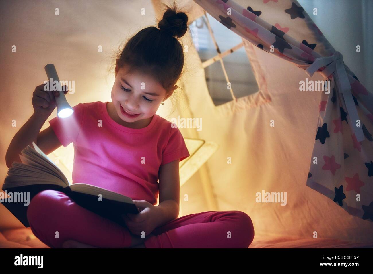 Cute little child is reading a book with flashlights in tent. Happy ...