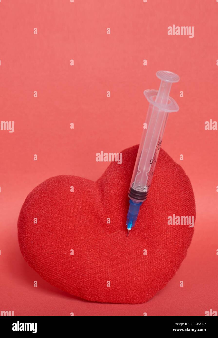 A stuffed toy heart with a syringe stuck in it. Red background ...