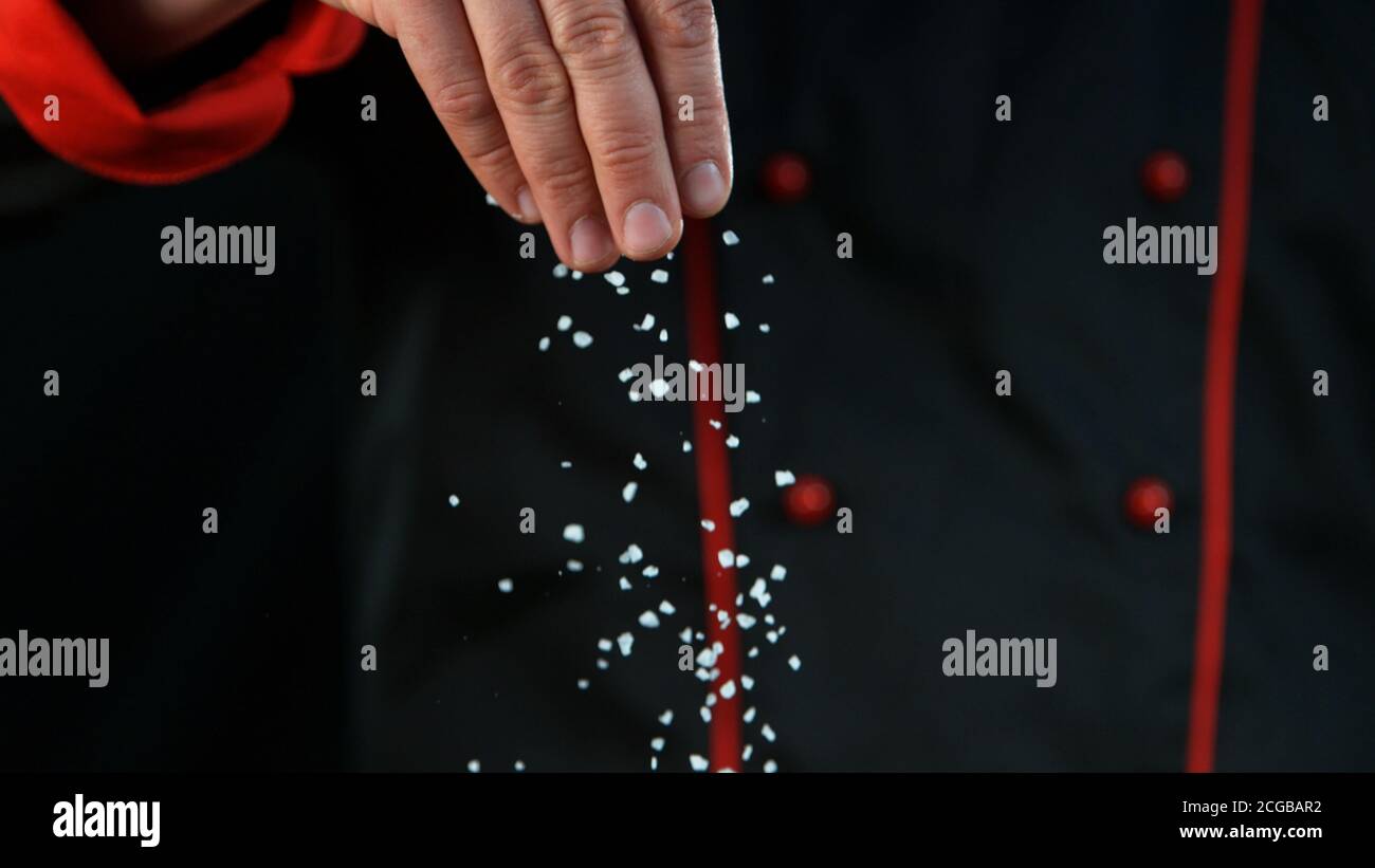 Closeup of chef pouring coarse-grained salt. Isolated on black ...