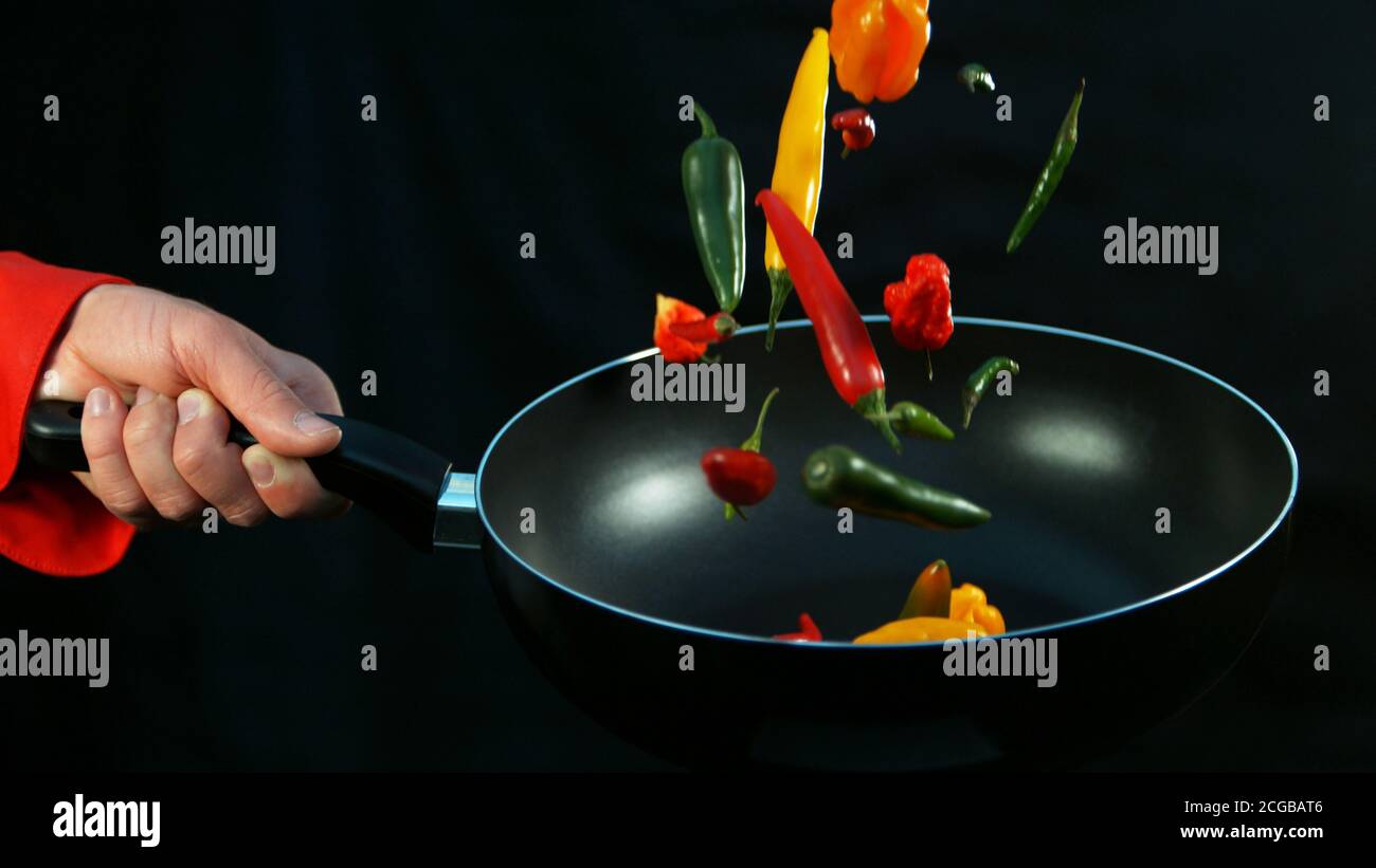 Closeup of chef holding frying with falling chilli peppers. Isolated on ...