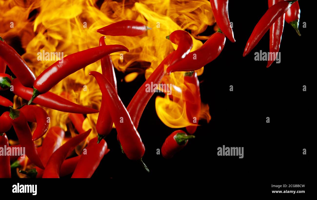 Flying red hot chilli peppers with flames, isolated on black background ...