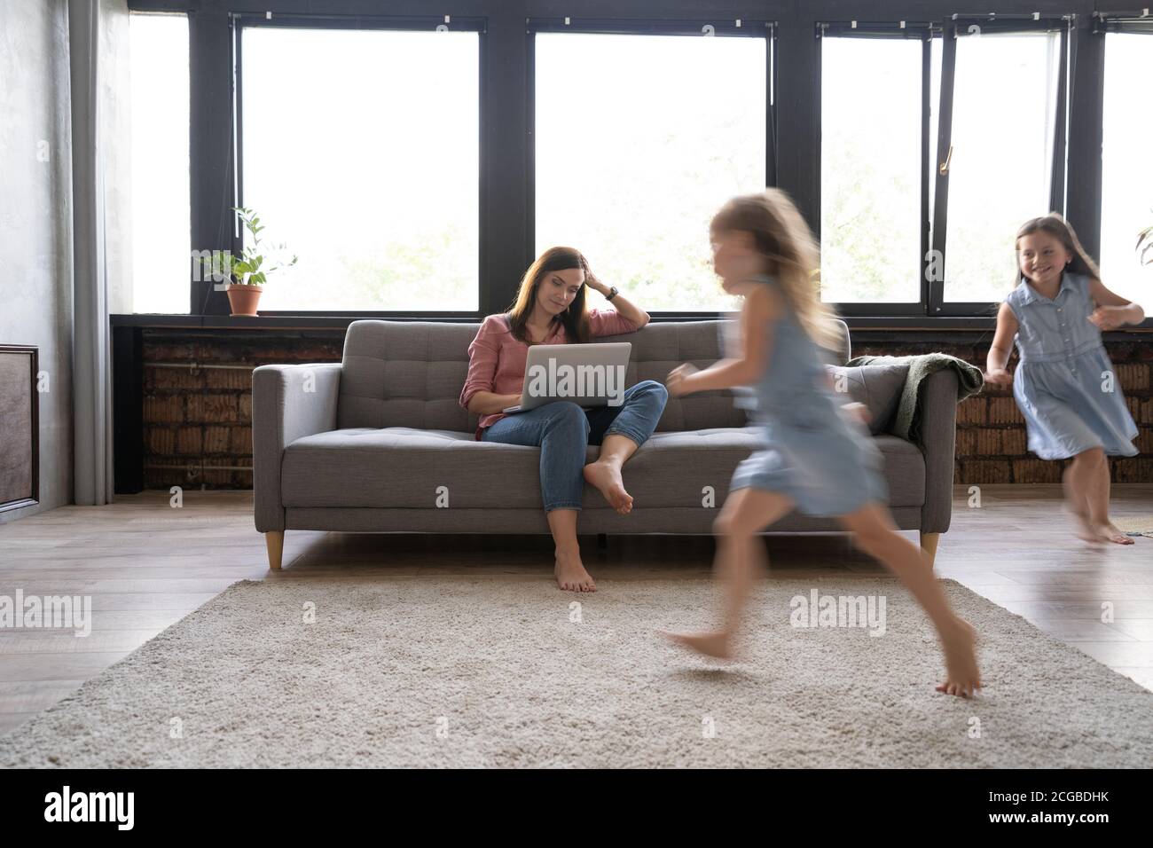 Young Single Mother Working On Laptop In Loft Sitting On Couch While