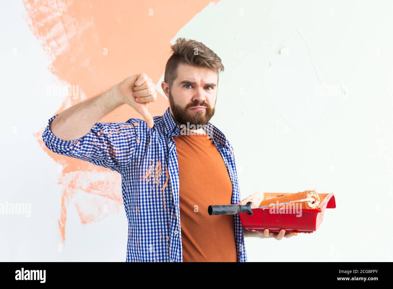 Sad man showing thumb down, male painting interior wall with paint ...