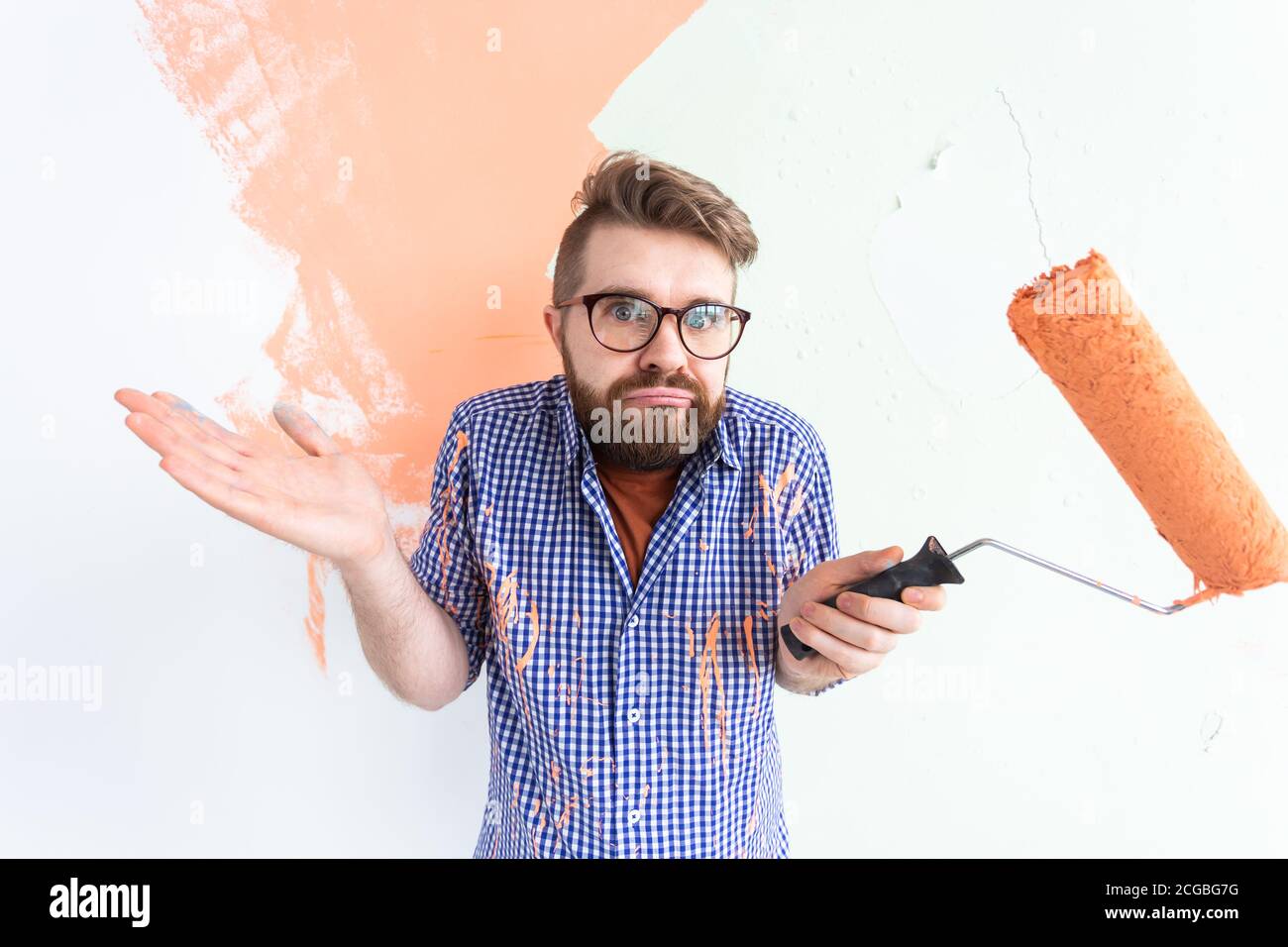 Confused man painting interior wall of home with paint roller ...