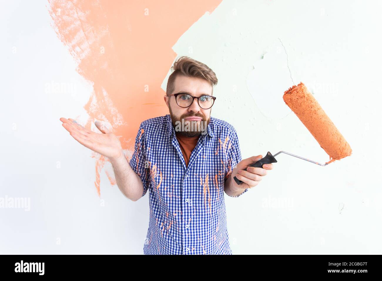Confused man painting interior wall with paint roller in new house. Guy ...