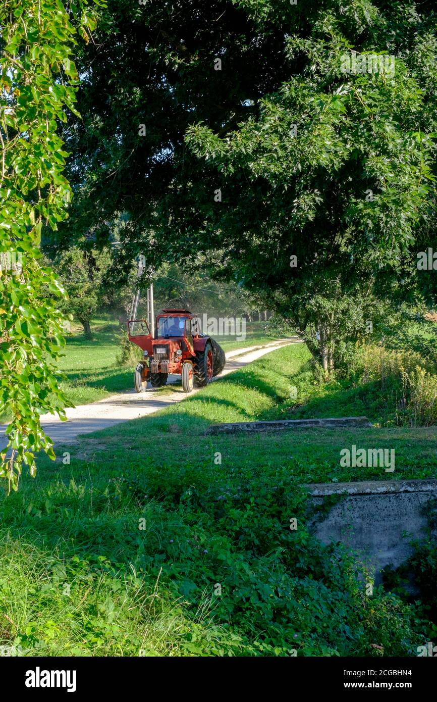 red tractor driving along rural country lane transporting large bale ...