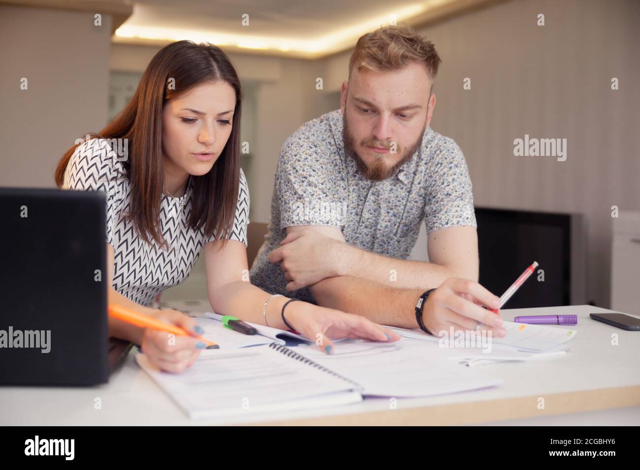 two young people, studying together, sitting in front of notes on a ...