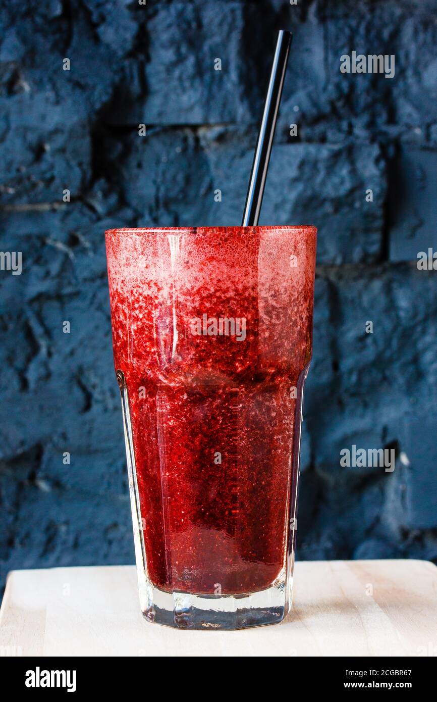 Red berry smoothie in a large glass glass against a dark stone wall ...