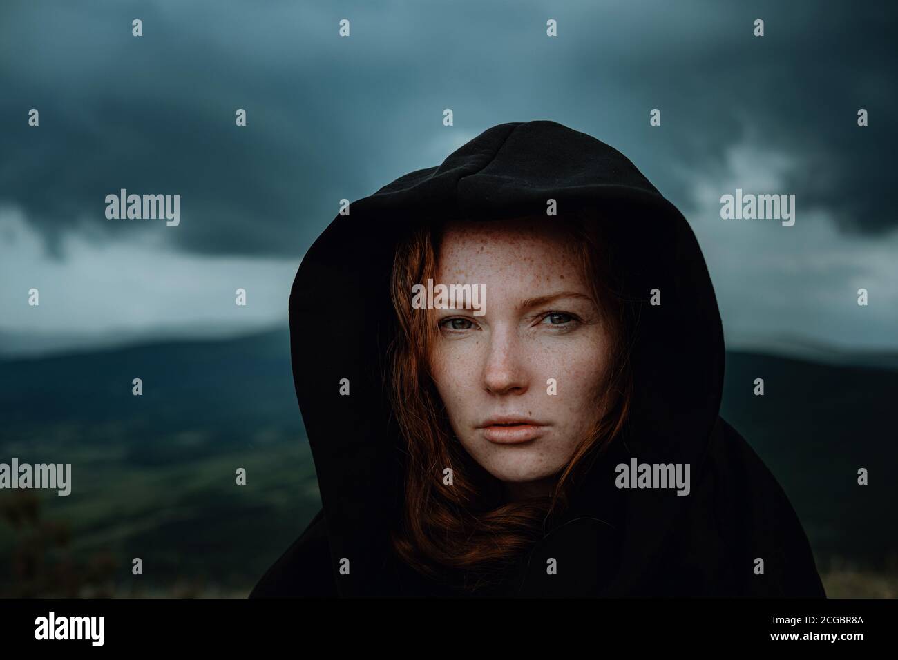 ginger woman in black hood stands in the rain. Dramatic and fantastic ...