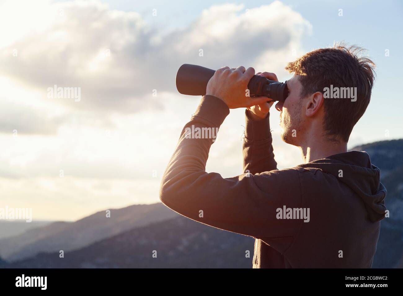 Young man at mountain looking through binoculars. Banner with copy ...