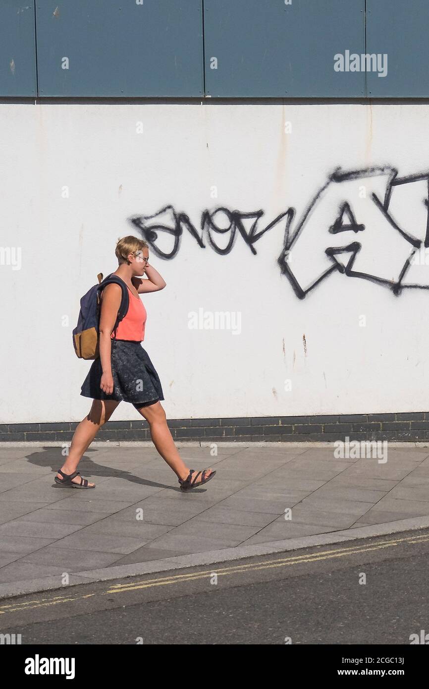 A woman walking past a wall sprayed with ugly graffiti tags in Newquay ...