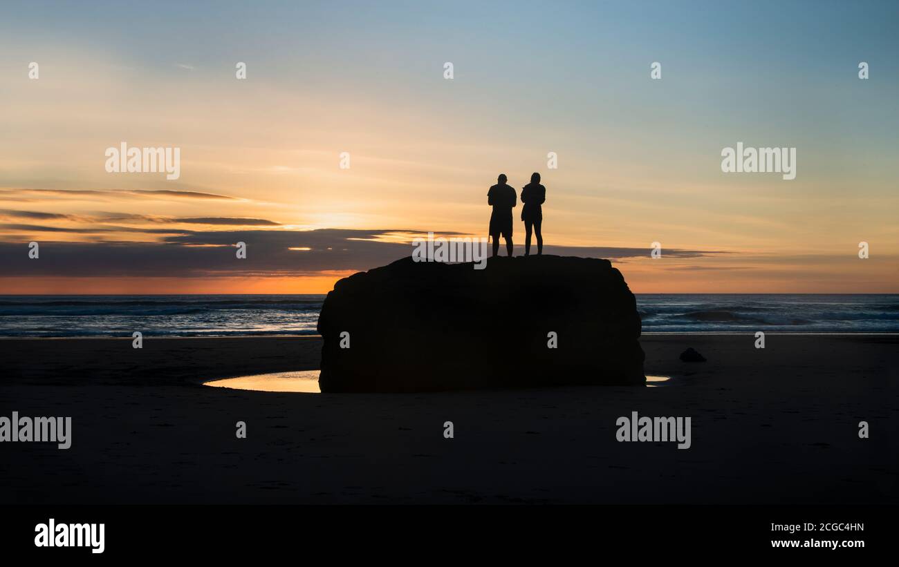 Silhouette image of two people standing on big rock and watching sunset ...