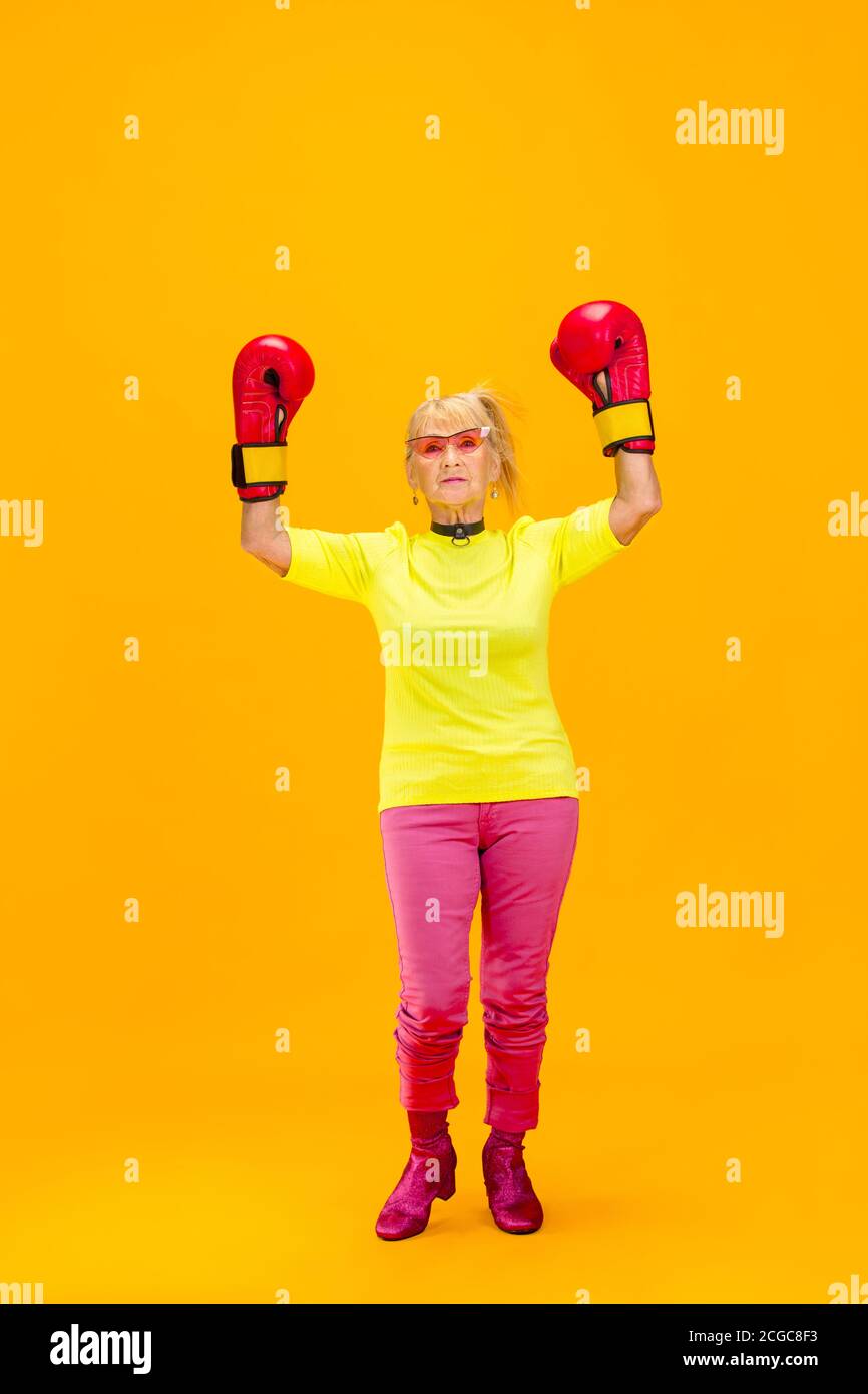 Boxing winner. Senior woman in ultra trendy attire isolated on bright ...