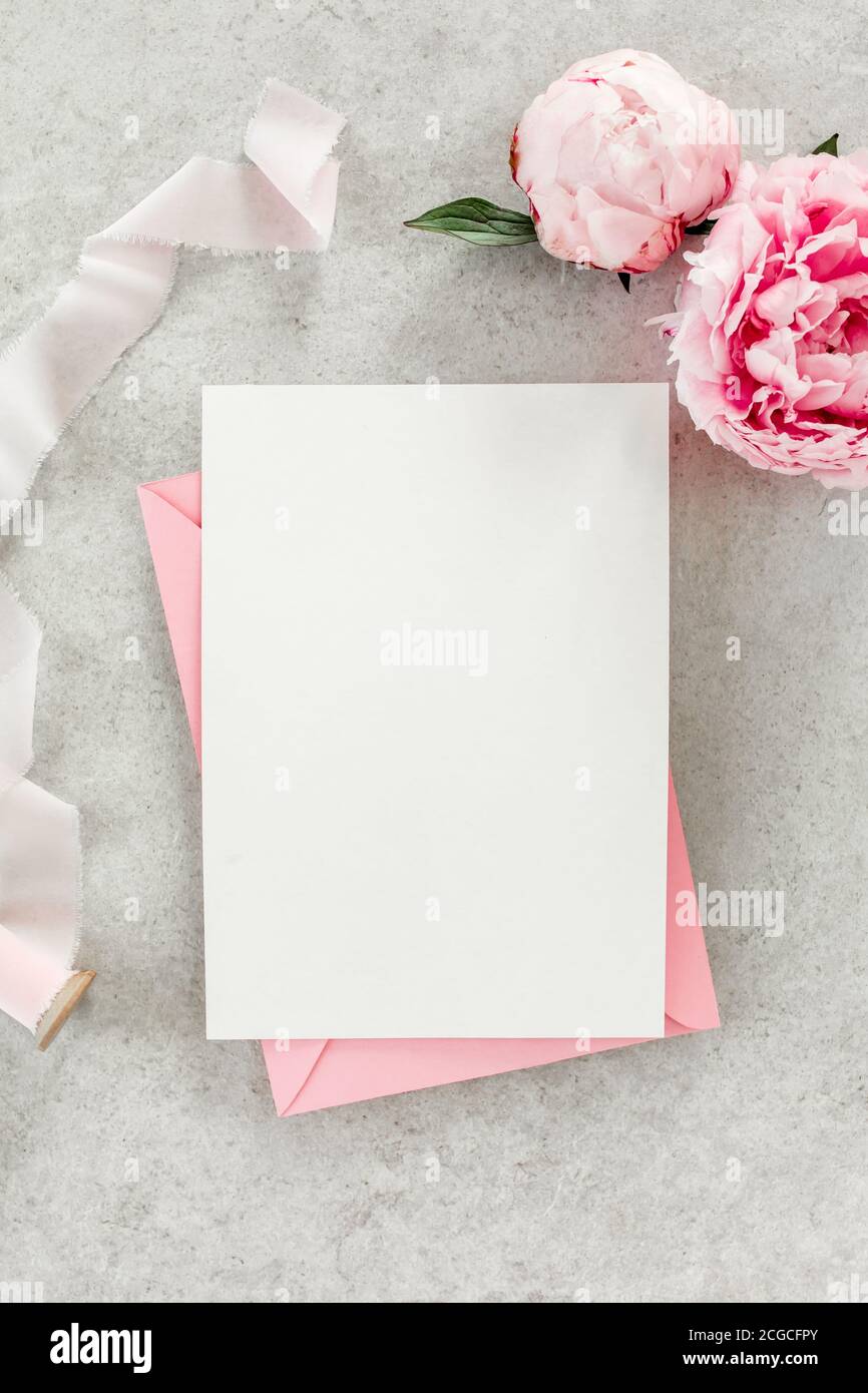 Mockup invitation, blank paper greeting card, pink envelope and peonies on gray stone table ...
