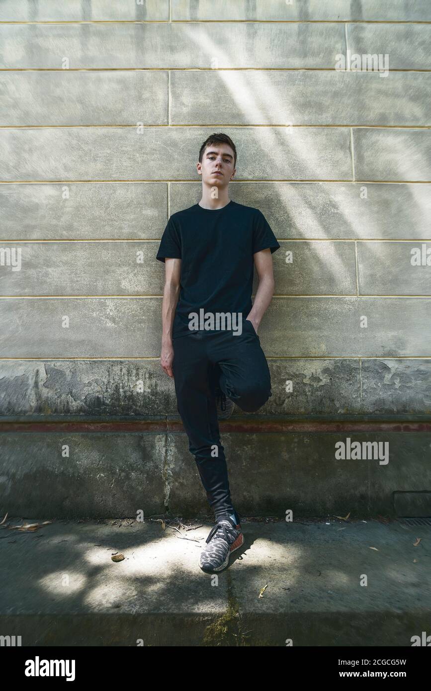 portrait of a cool, standing young man who is leaning against a wall ...
