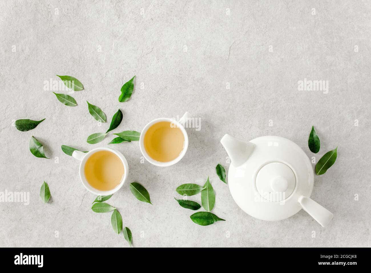 Herbal tea with two white tea cups and teapot, with green tea leaves ...