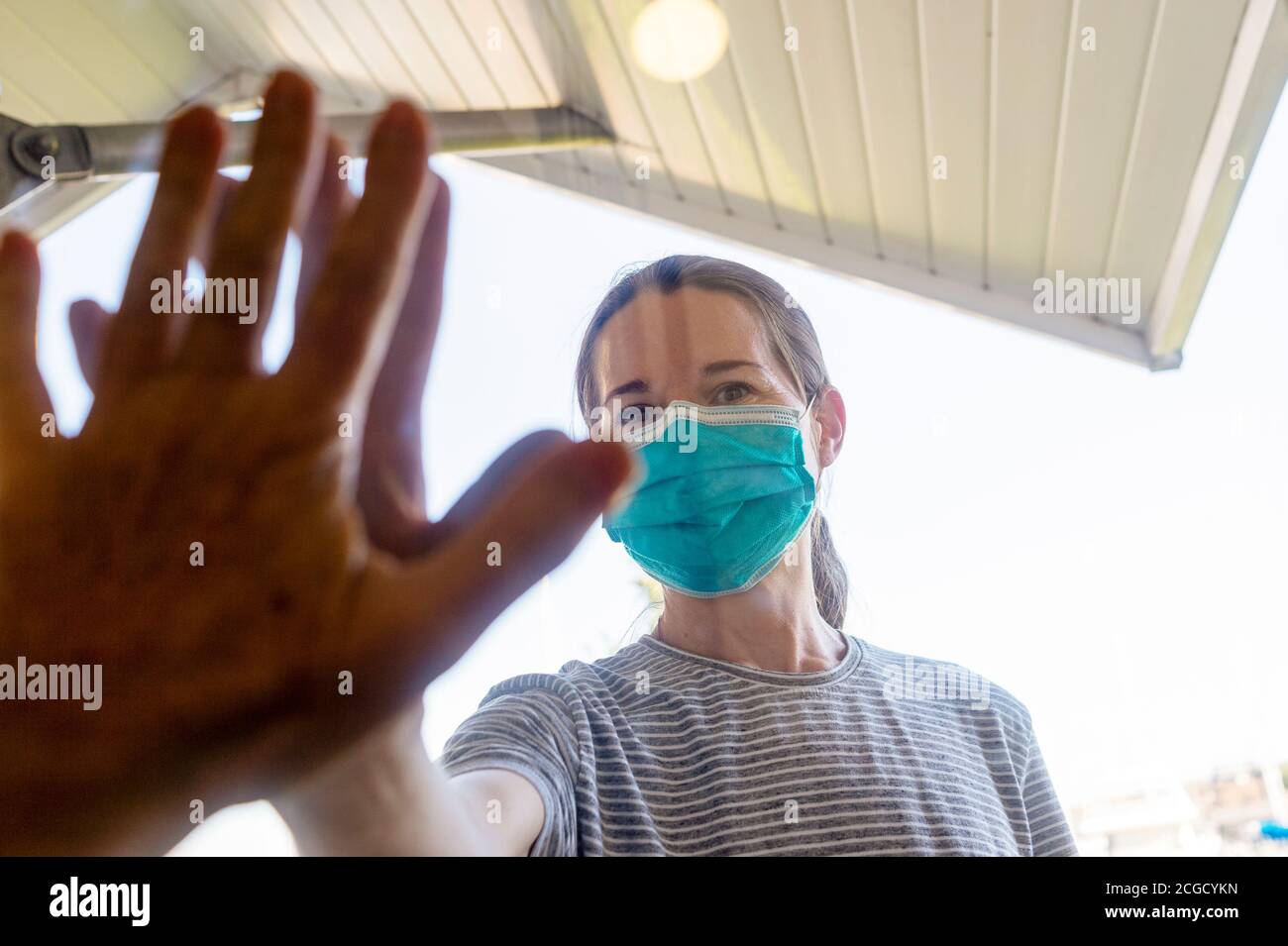 Woman wearing a medical face mask, touching hands through a window ...