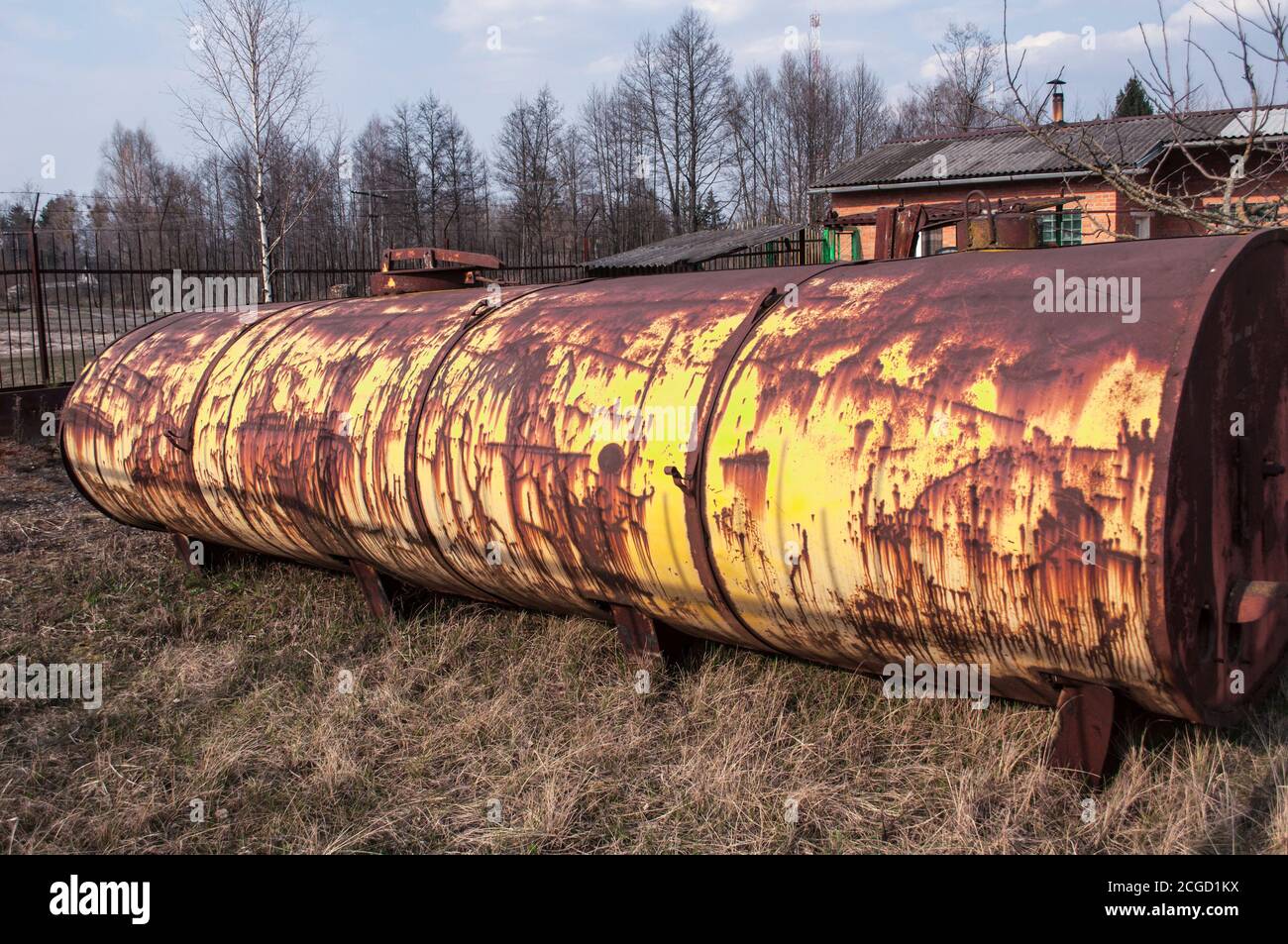 Big, yellow, rusty tank on nature background and red brick house behind ...