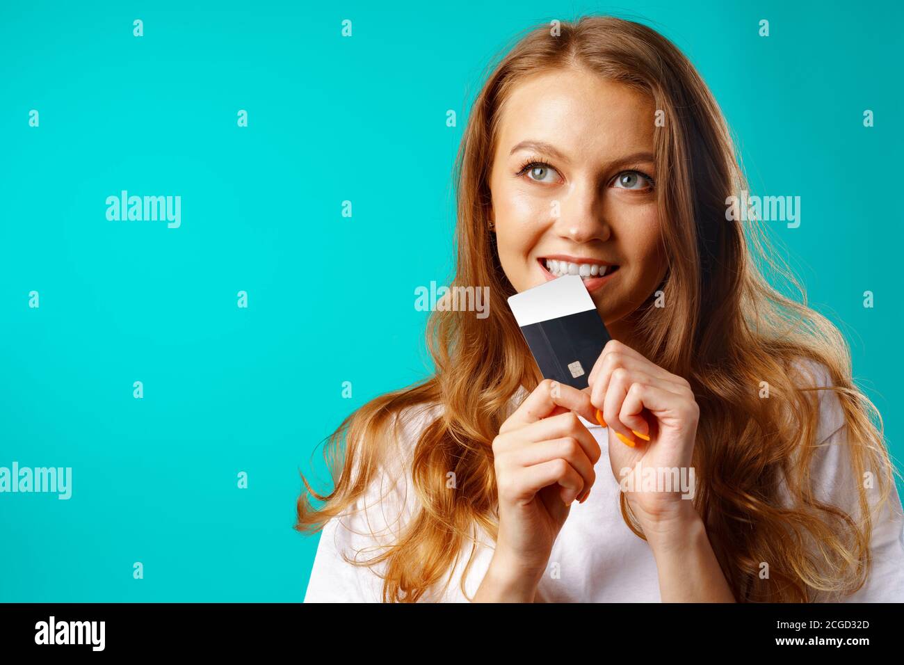 Smiling young woman biting a credit card within temptation of shopping ...