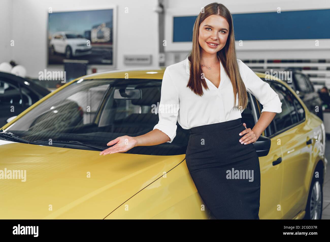 Attractive young female car dealer standing in showroom Stock Photo - Alamy