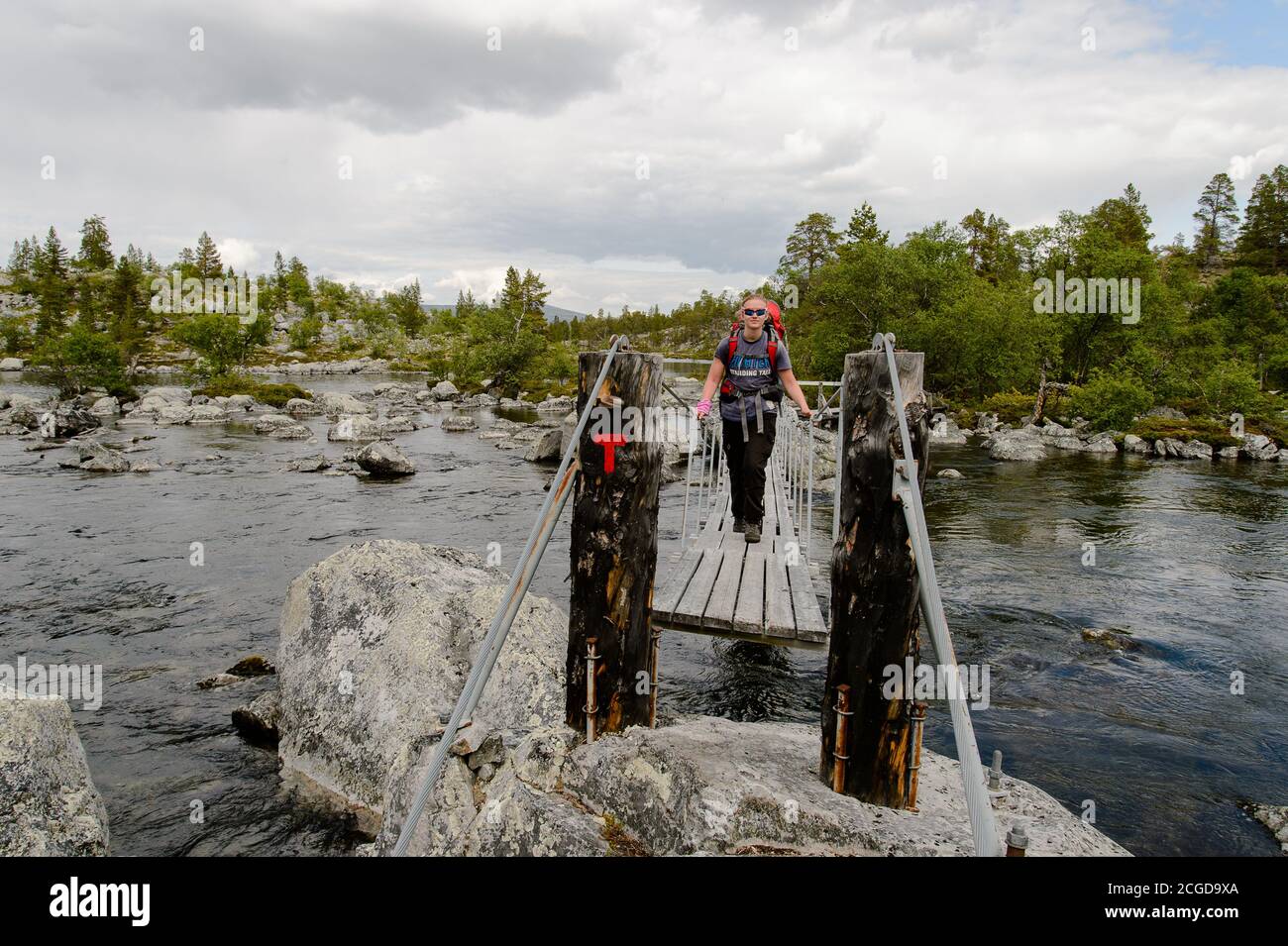 Pretty young girl with backpack crossing river og suspension bridge in ...