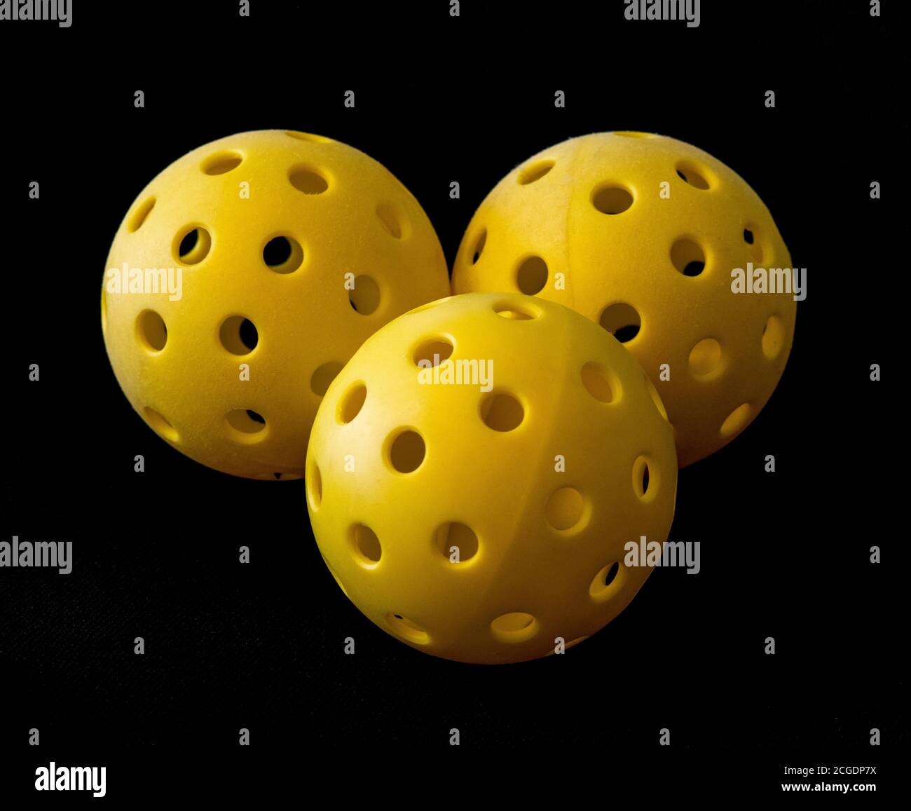 Three pickleballs over a black background. Pickleball has become the ...