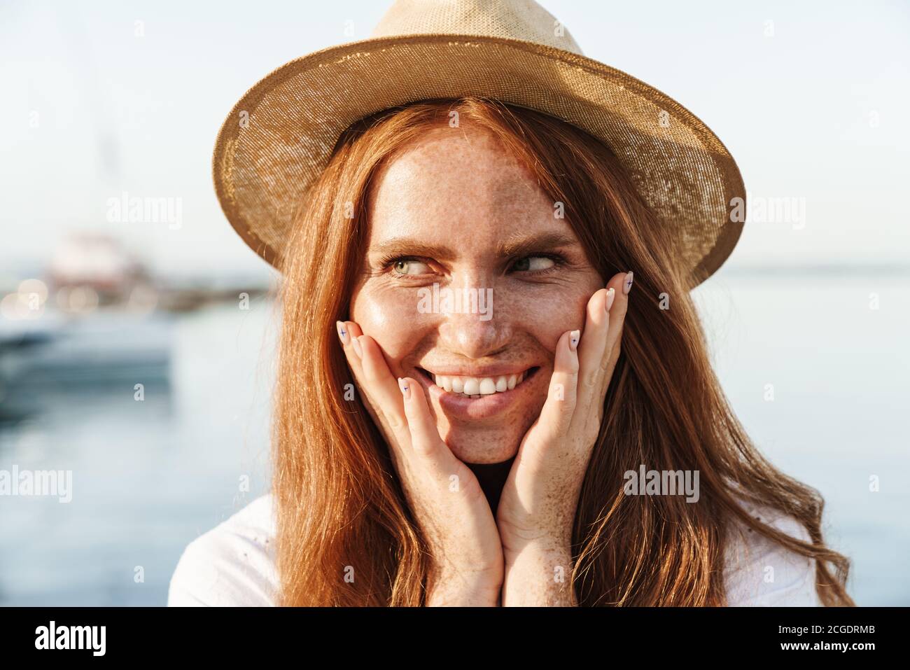 Image of joyful ginger woman in hat smiling and looking aside while ...
