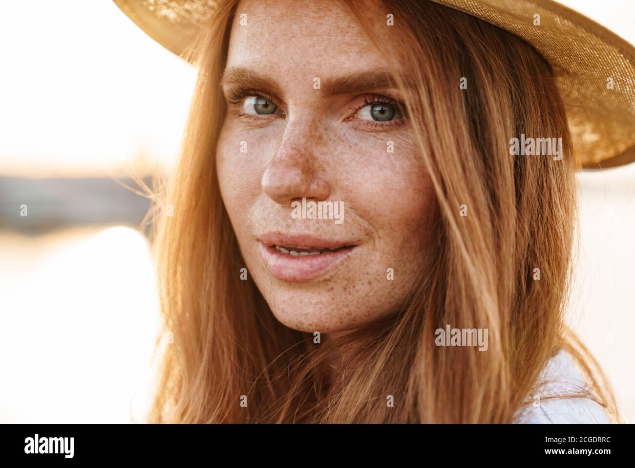 Image of pleased ginger woman in hat posing and looking at camera while ...