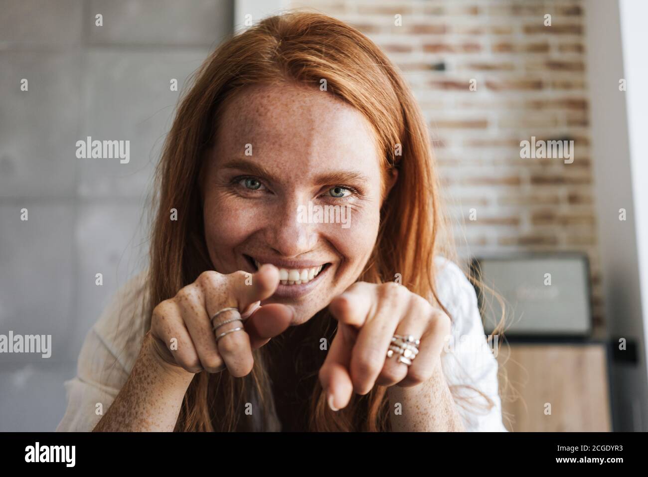 Image of happy ginger woman with freckles smiling and pointing fingers ...