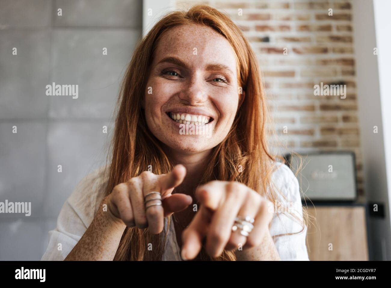 Image of happy ginger woman with freckles smiling and pointing fingers ...