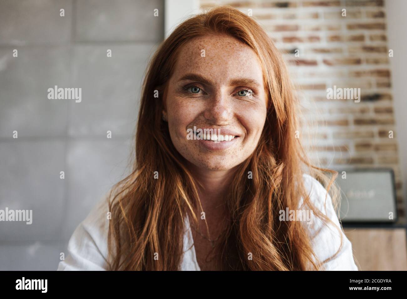 Image of happy ginger woman with freckles smiling and looking at camera ...