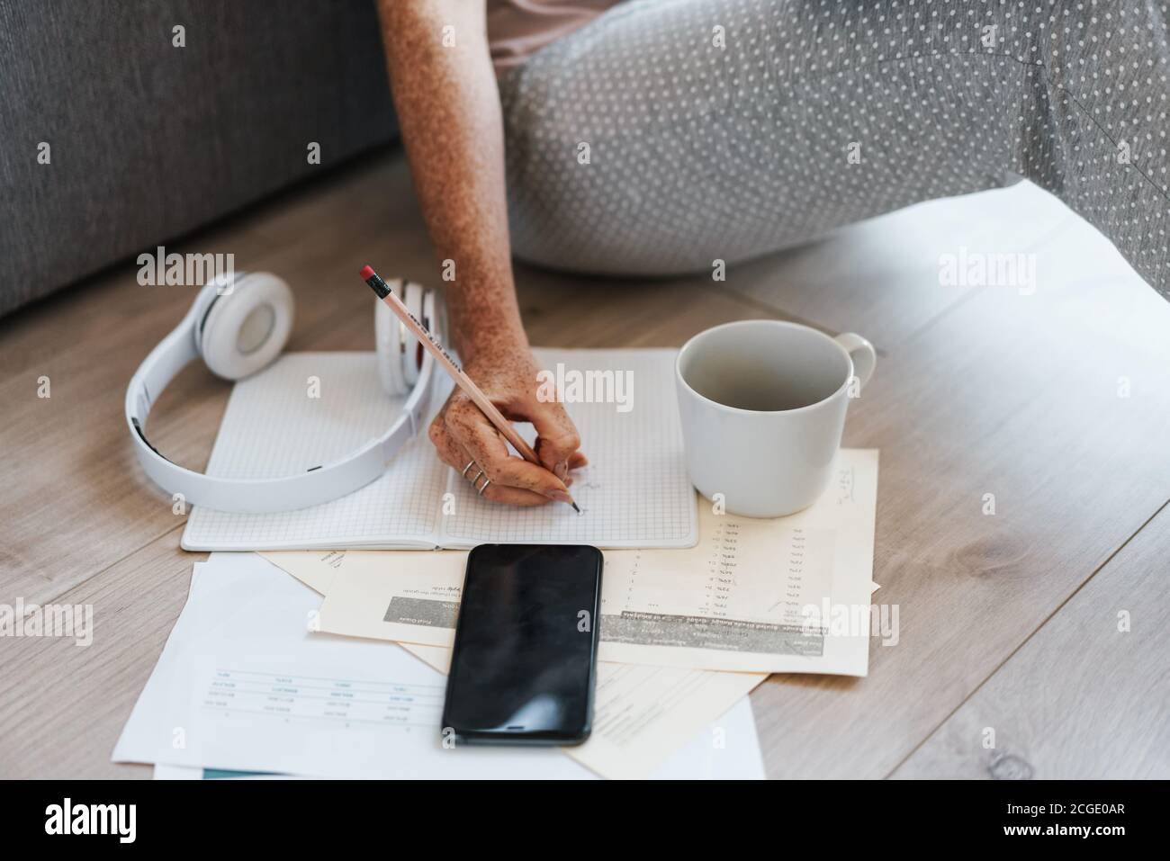Cropped image of woman writing down notes while sitting on floor at ...