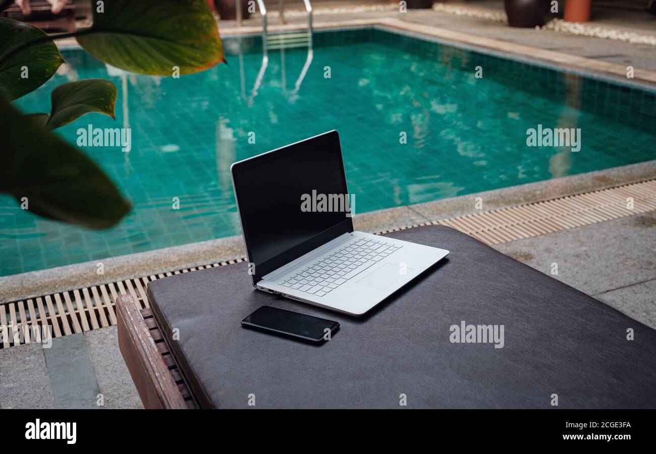 White Laptop at the swimming pool and smartphone, workspace at a ...