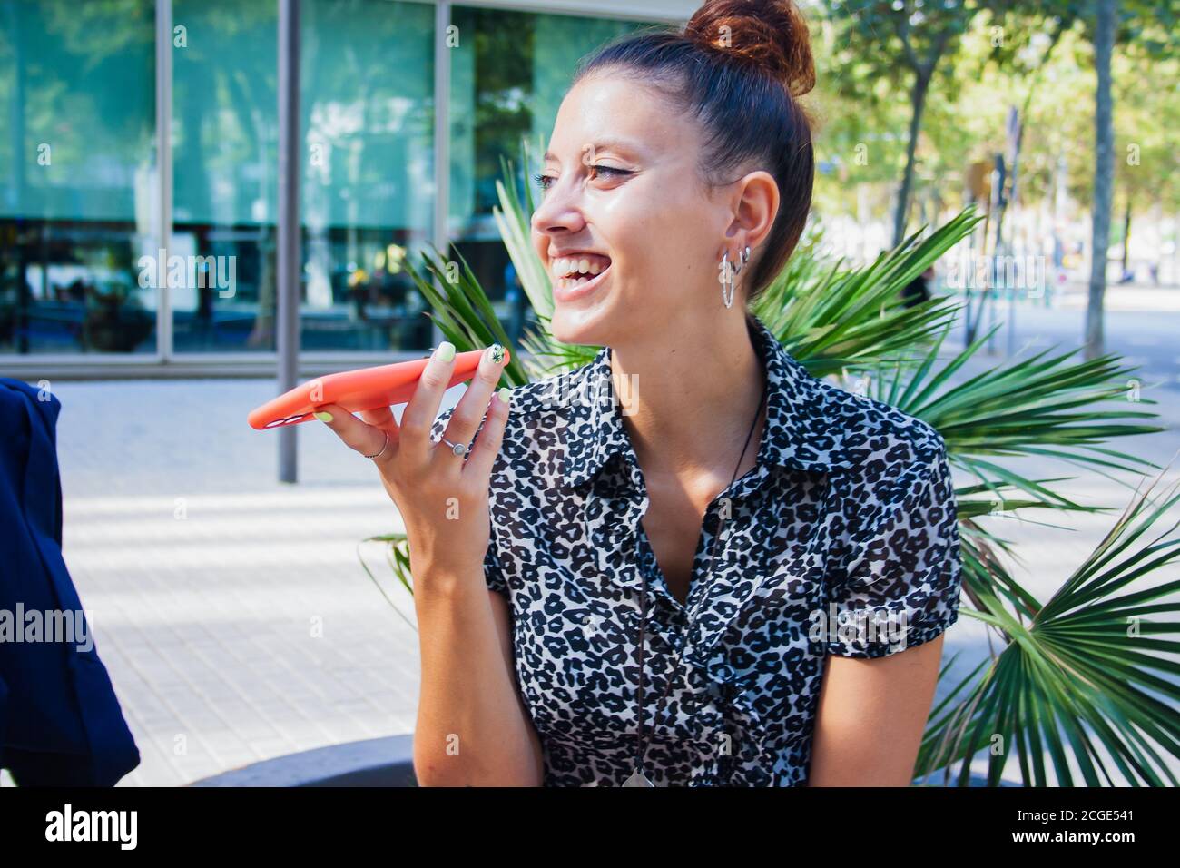 Working young woman making a voice note on her phone and laughing ...