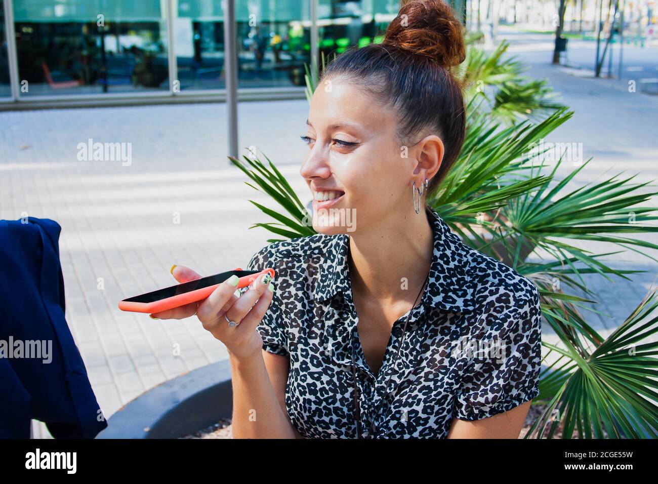 Working young woman making a voice note on her phone sitting outside of ...