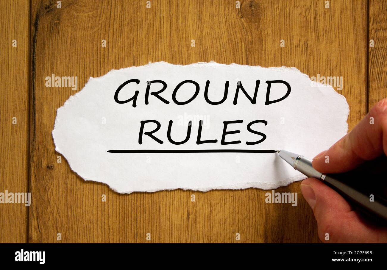 Male hand writing 'ground rules' on white paper on wooden table ...
