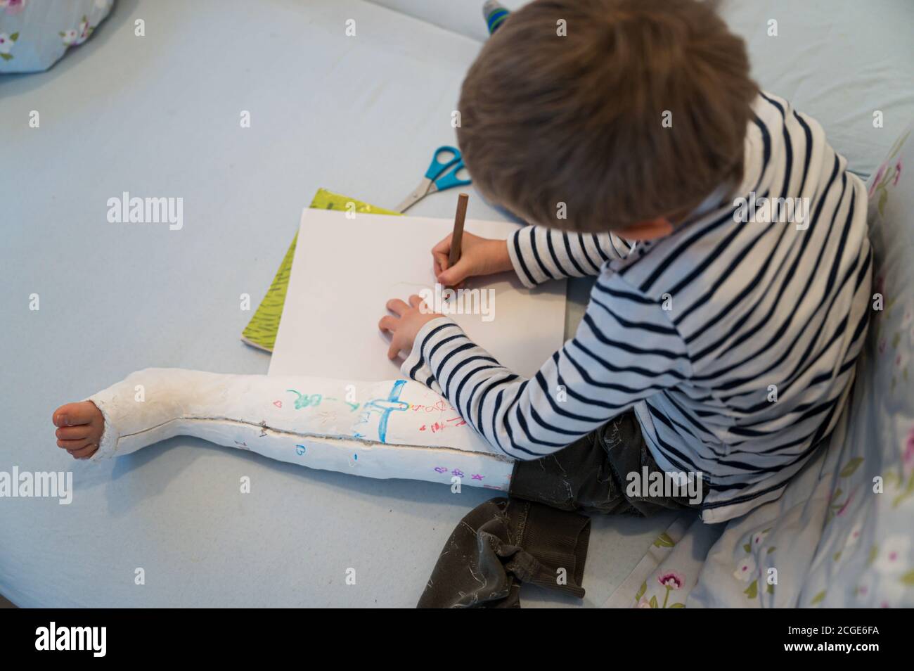 Aerial view of toddler boy with his leg in a cast drawing on white ...