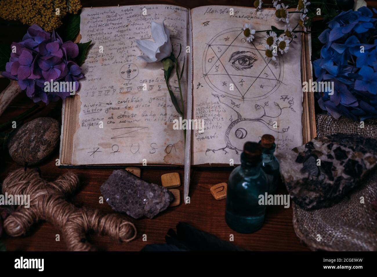 Open old book with magic spells, runes, black candle and herbs on witch ...