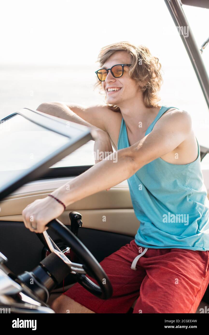 Young blond man steers speed motor boat on the sea during sunset. Sea ...
