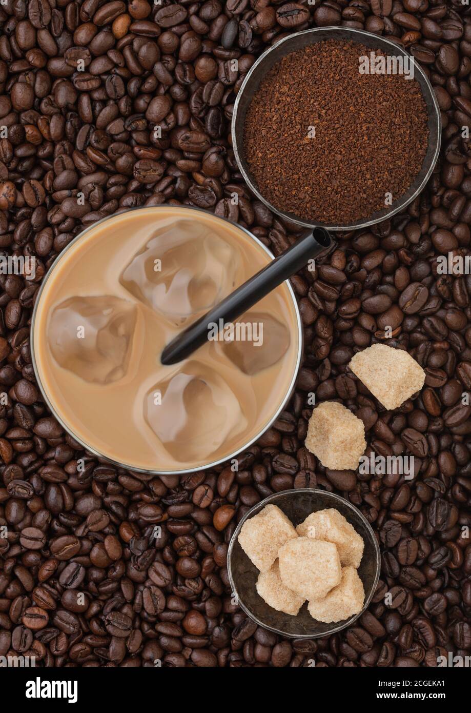 Glass of cold coffee with ice cubes and straw on fresh raw coffee beans ...