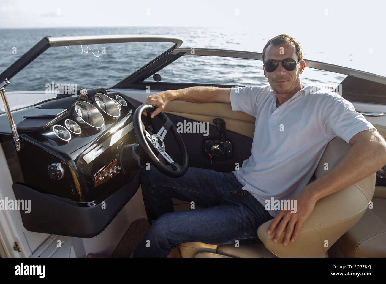 The proud male owner of a luxury speedboat sits at the steering wheel ...