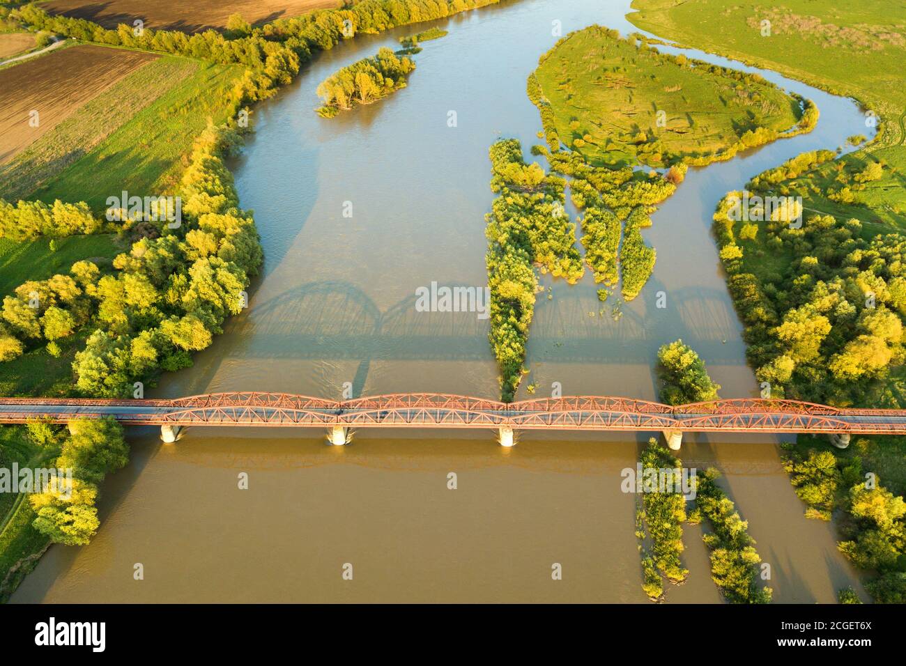 Aerial view of a narrow road bridge stretching over muddy wide river in ...