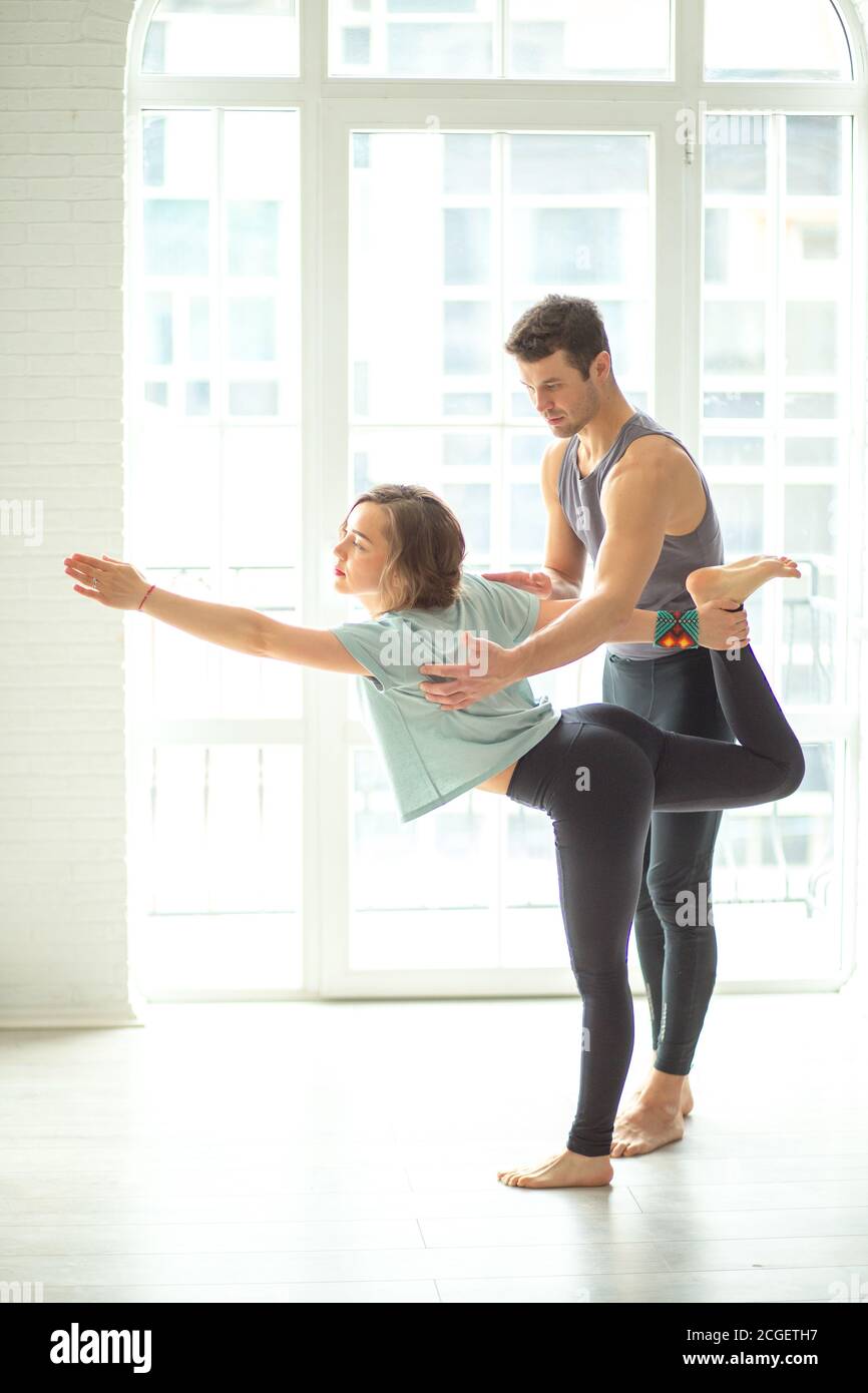 Professional Yoga male instructor helps female beginner to make asana ...