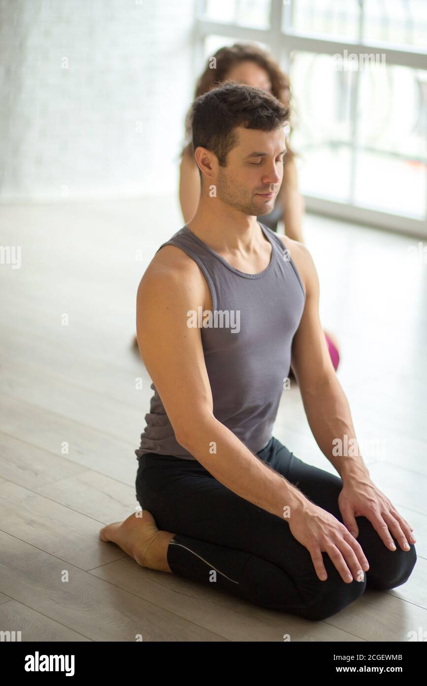 Young sportive male instructor practicing yoga with group of young ...