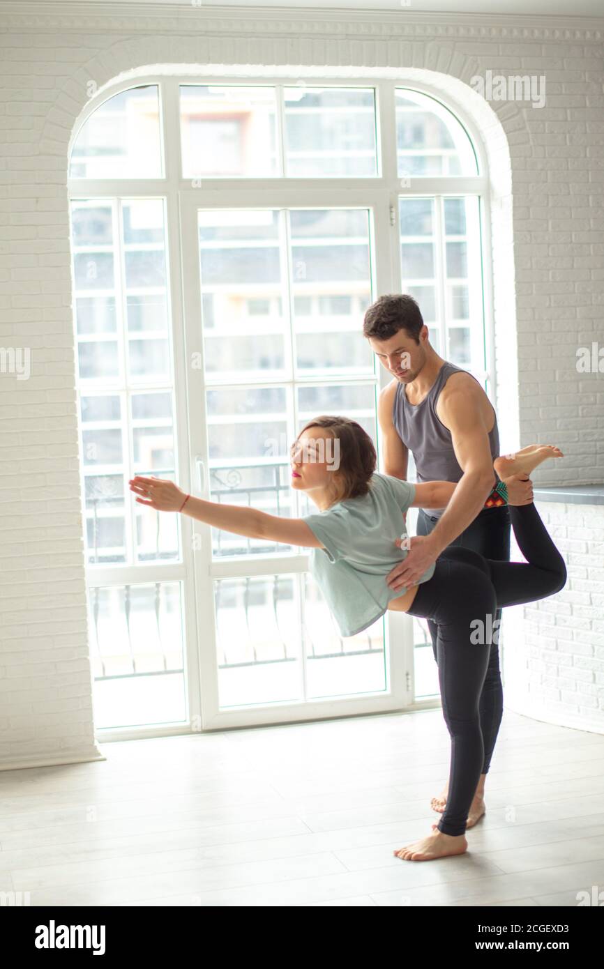 Professional Yoga male instructor helps female beginner to make asana ...