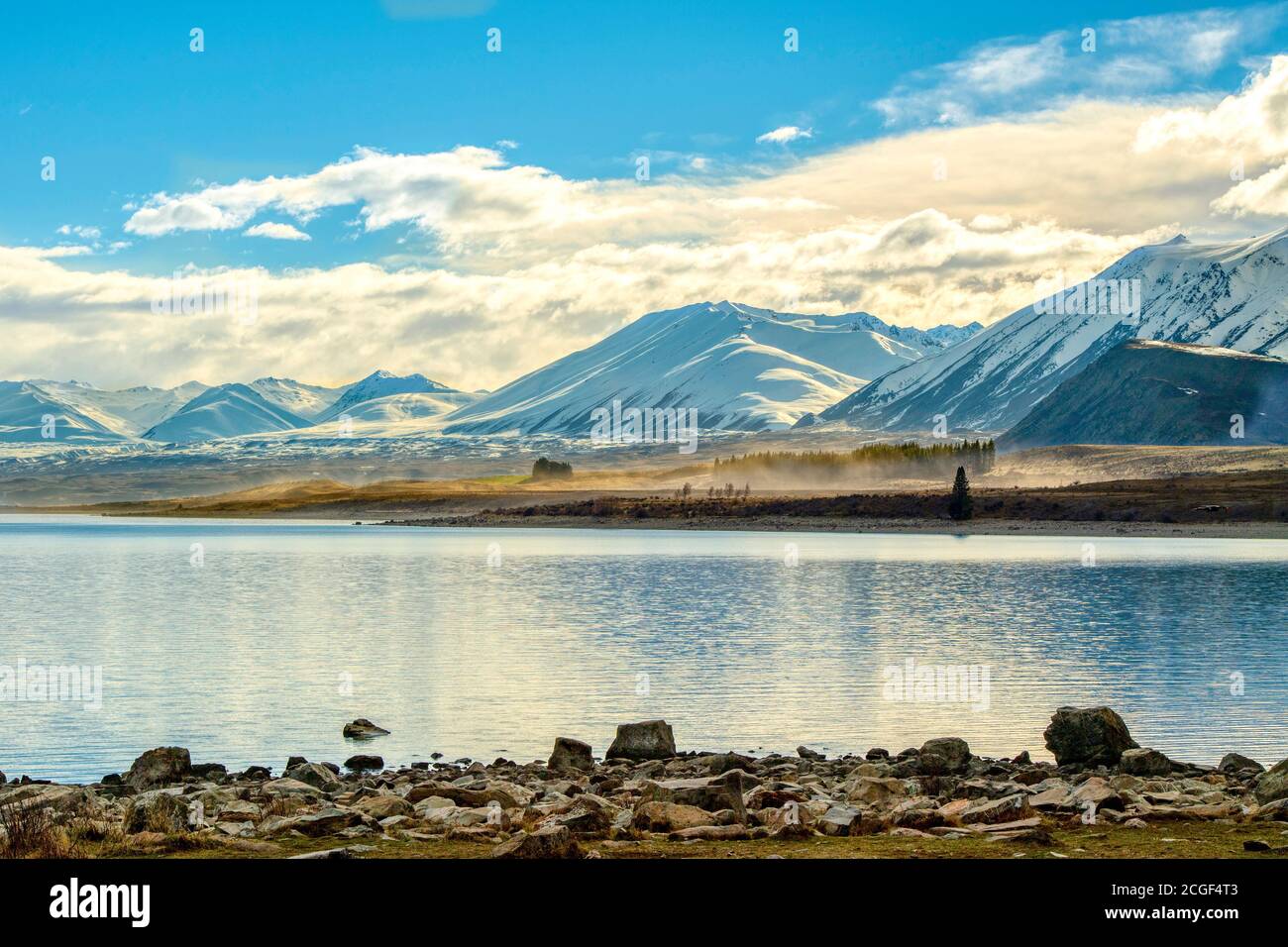 Snowy mountains and pine trees, cars running on gravel road causing ...