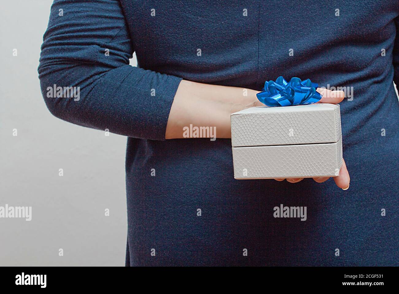 Woman with a gift behind her back on a white background Stock Photo - Alamy