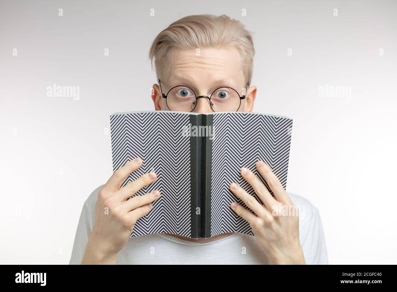 Amazed young blond student male with bugged eyes covering his mouth ...