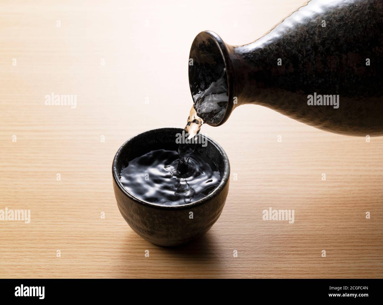 Pouring sake into a sake cup set against a wooden backdrop Stock Photo ...